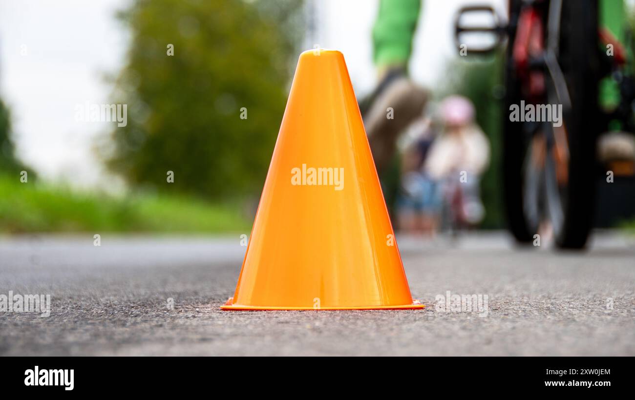 An orange traffic cone sits prominently on a sidewalk, while children ...