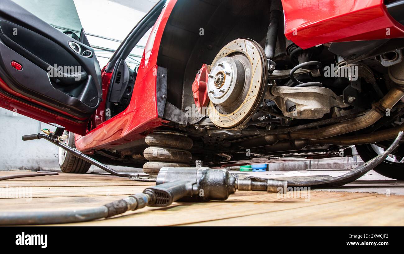 A red sports car is elevated on a hydraulic lift, exposing its ...