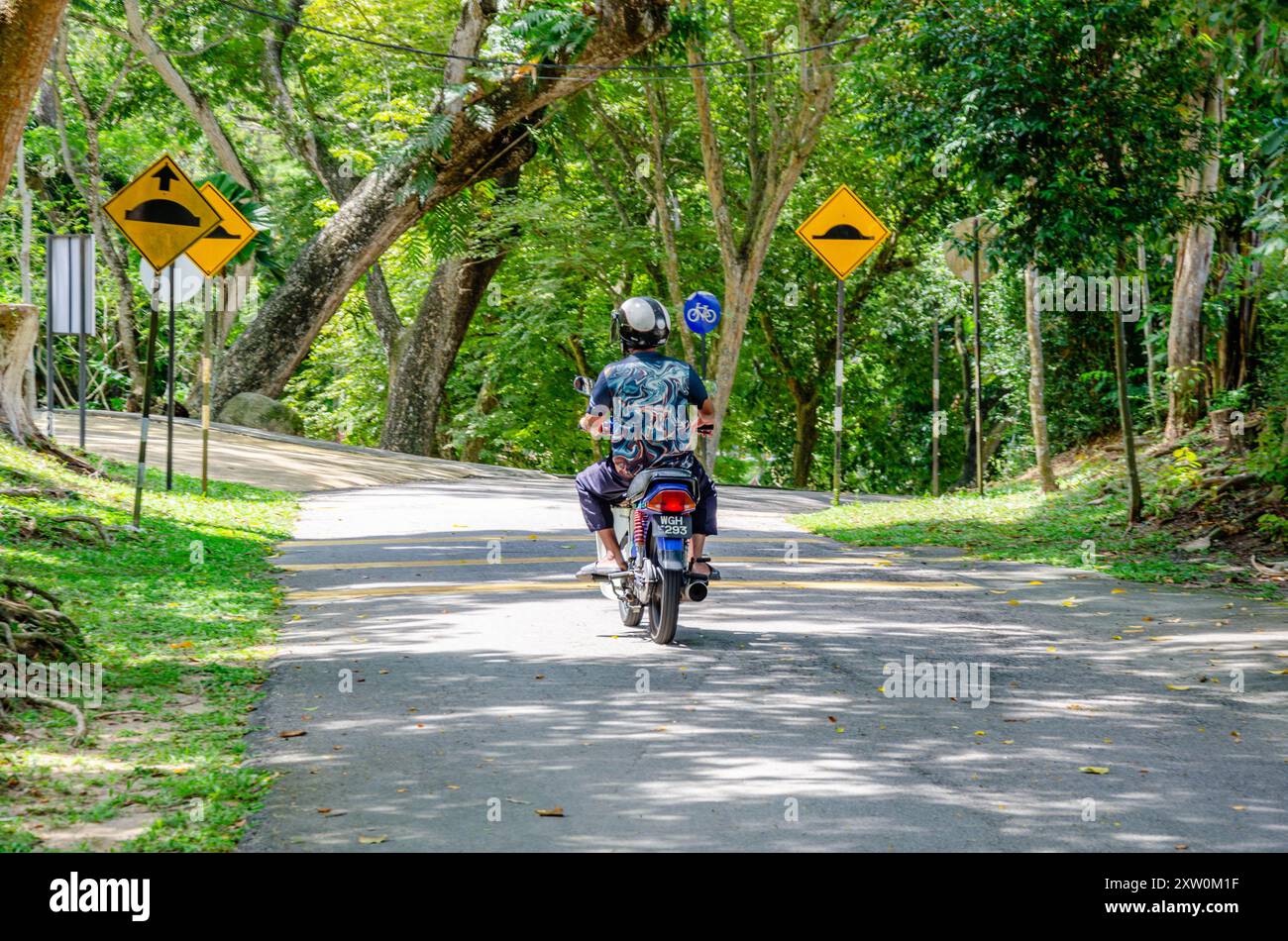 A man rides a scooter past signs warning of speed bumps on a road in ...