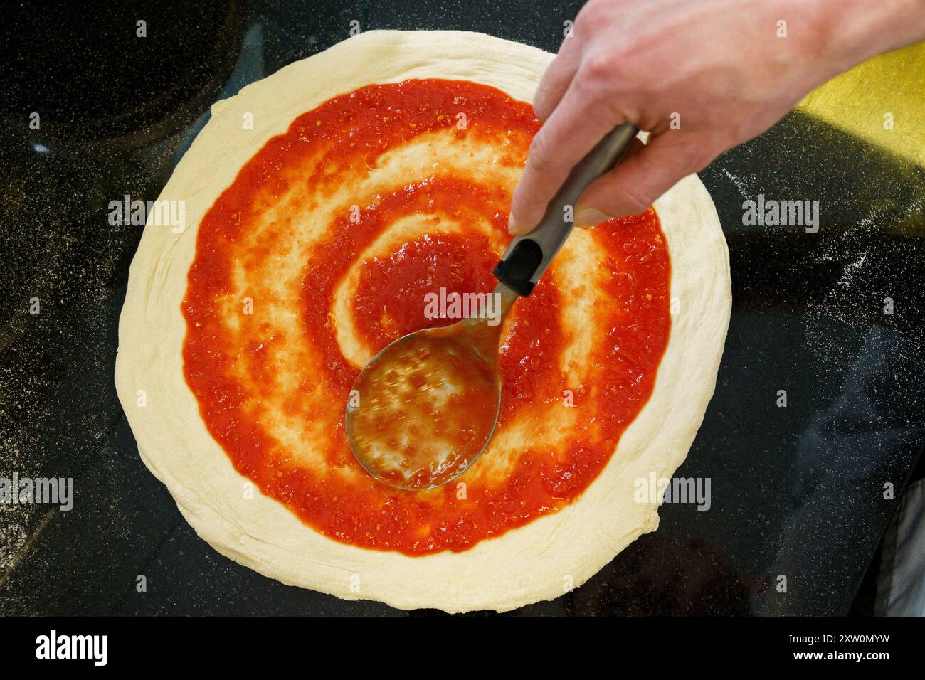 Top down view of spreading tomato sauce on pizza dough with a spoon ...