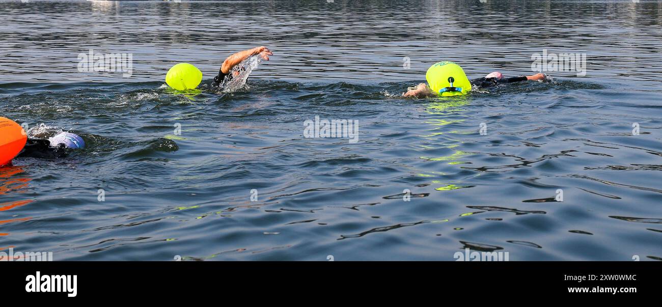 Three swimmers wearing colorful flotation devices swimming together in ...
