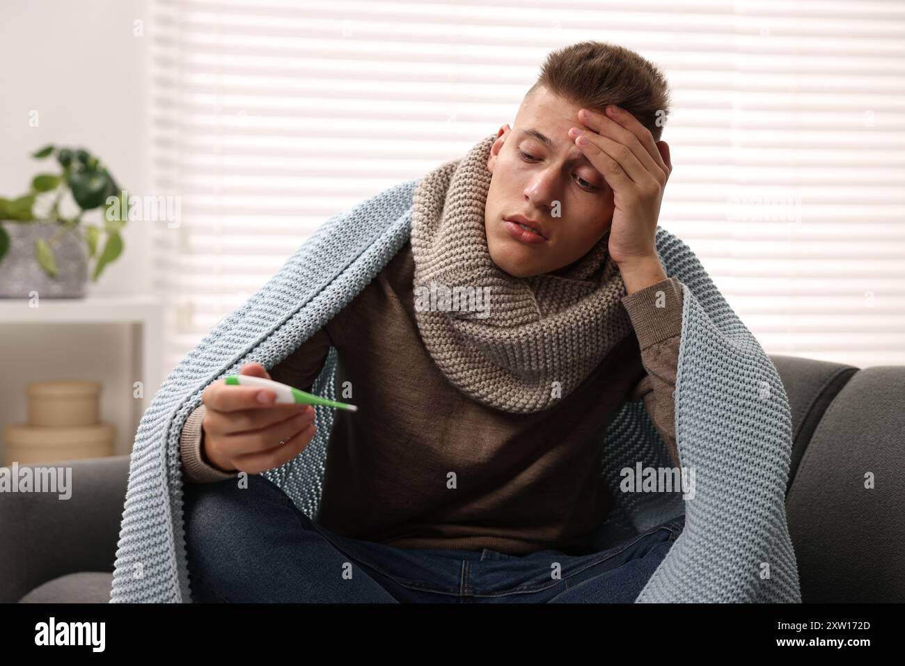Cold symptom. Young man checking temperature with thermometer at home ...