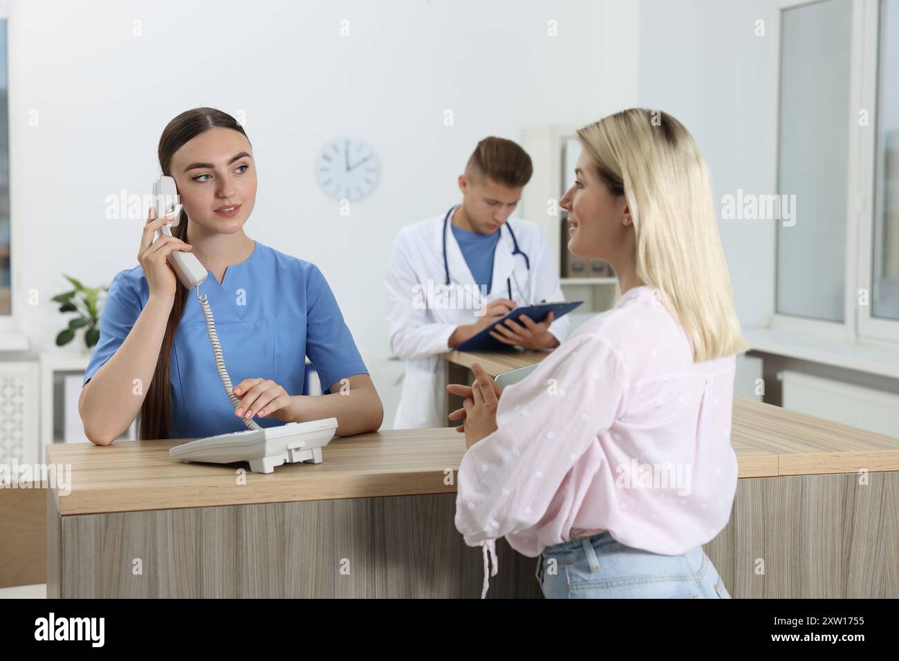 Professional receptionist and doctor working with patient at wooden ...