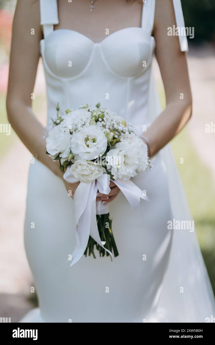 Elegant bride holding a white floral bouquet in a minimalist wedding ...