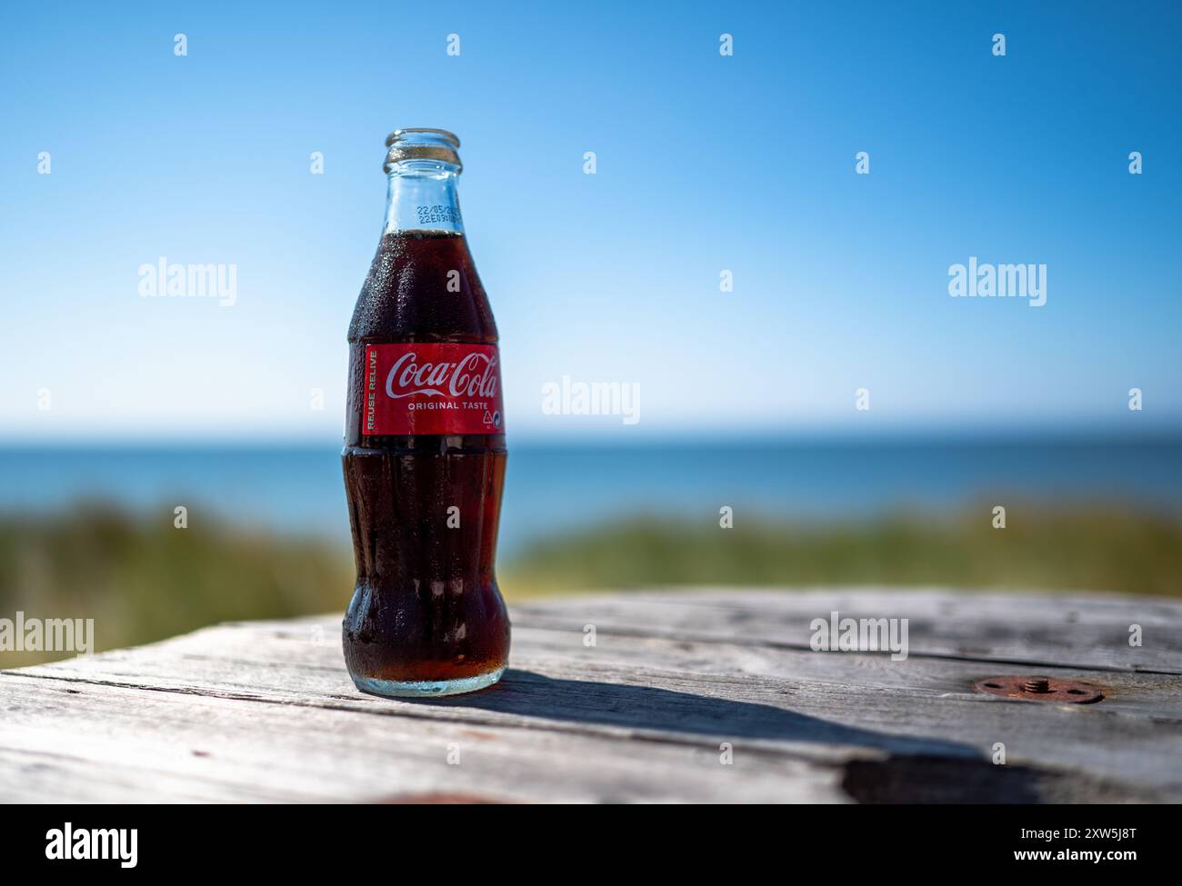 A coca-cola bottle against a sea and blue sky background in summer ...