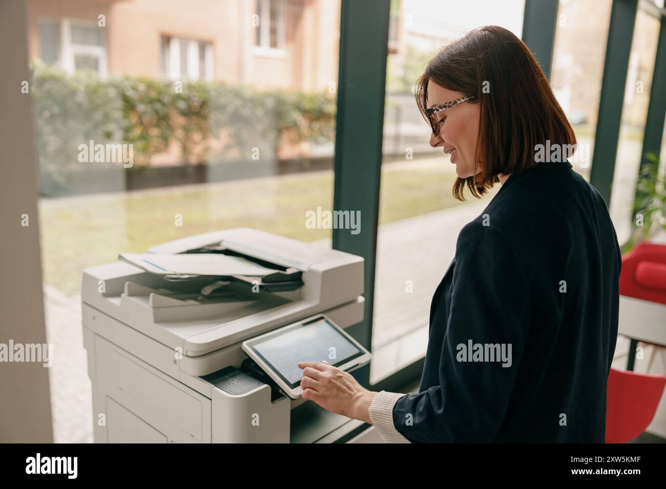 A woman is using a copier in a modern office with glass windows for ...