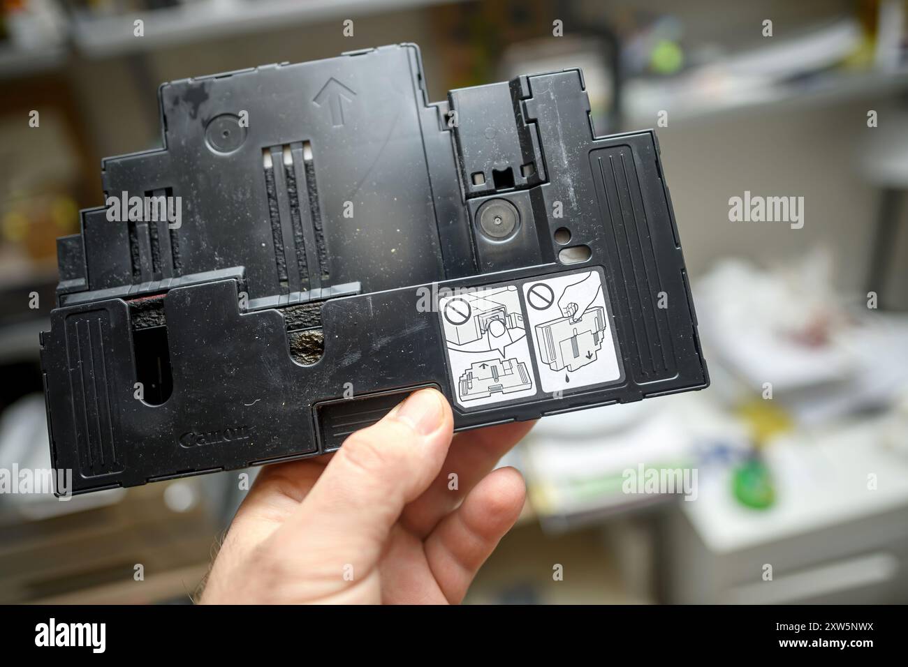 A hand holding a dusty black plastic printer part with instructional ...