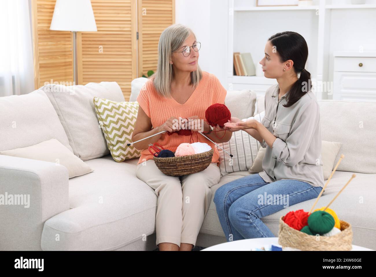 Daughter talking to her mother while she knitting on sofa at home Stock ...