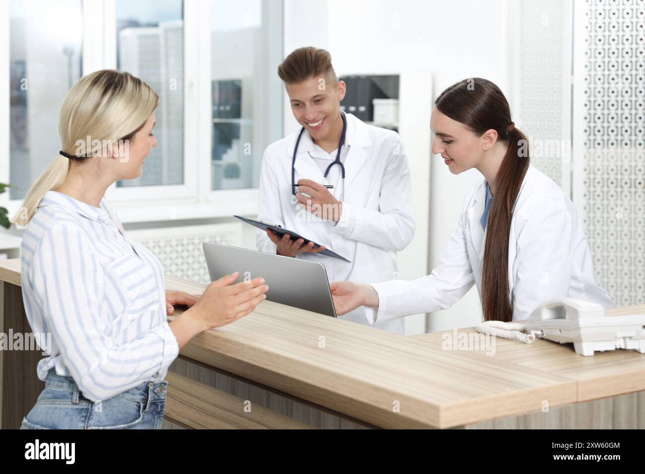 Professional receptionist and doctor working with patient at wooden ...