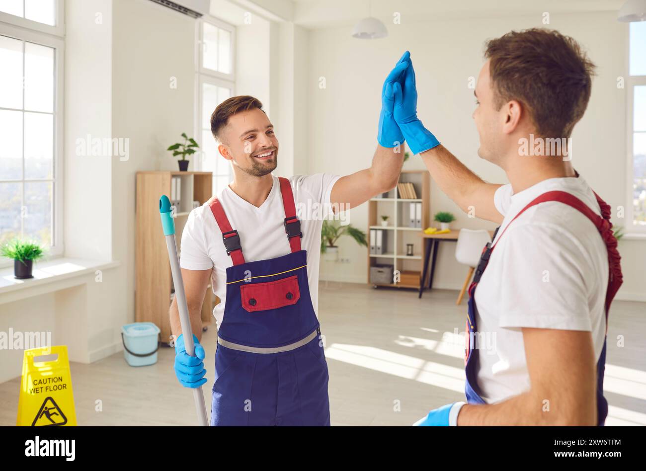 Two happy workers from cleaning service high five each other after they ...