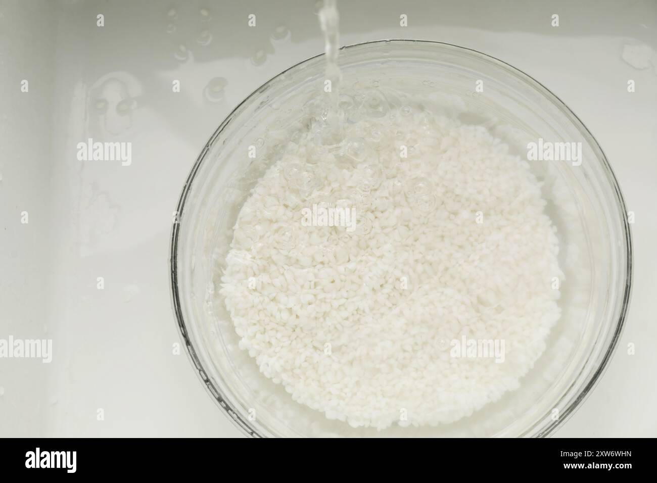 Pouring water into bowl with rice in sink, top view Stock Photo - Alamy