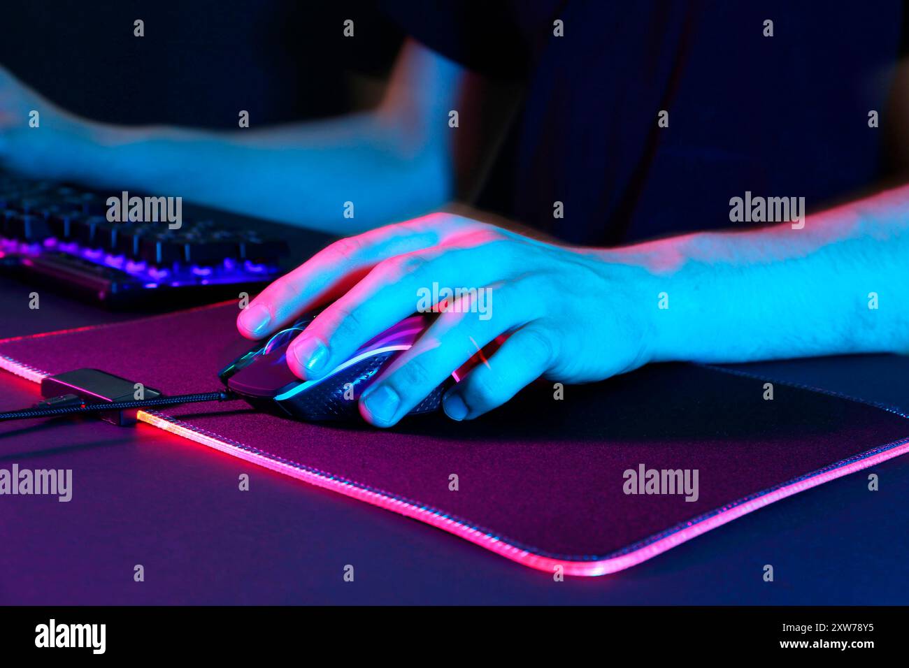 Gamer using modern wired computer mouse in neon lights at dark table ...