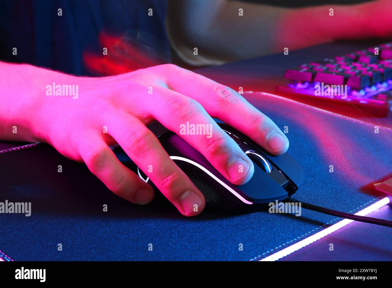 Gamer using modern wired computer mouse in neon lights at dark table ...