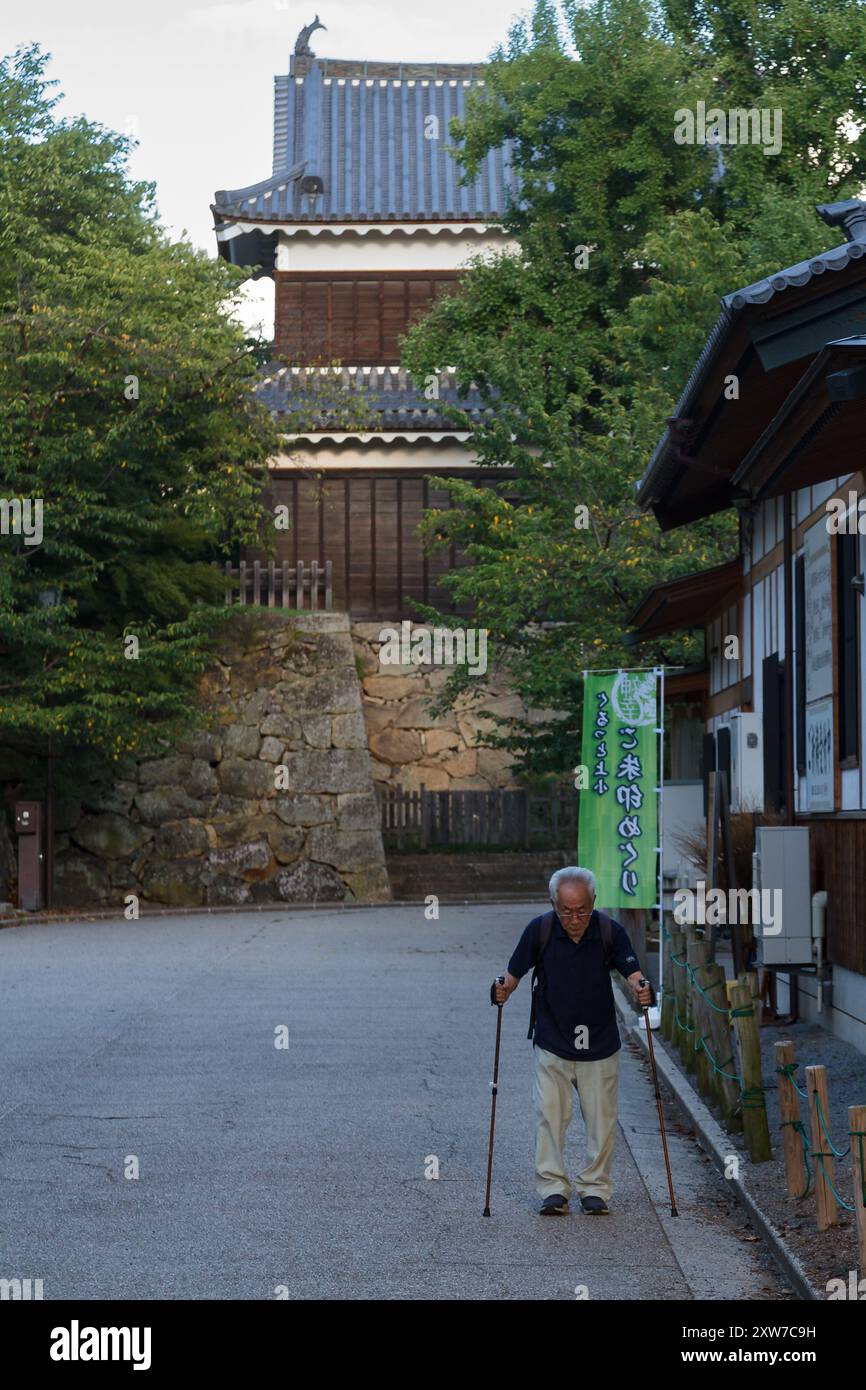 An older Japanese man uses trekking polers as he walks in the grounds ...