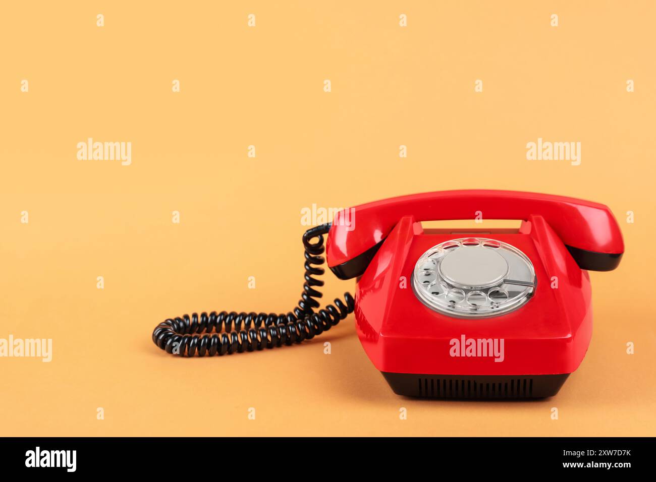 One red telephone with handset on pale orange background, space for ...