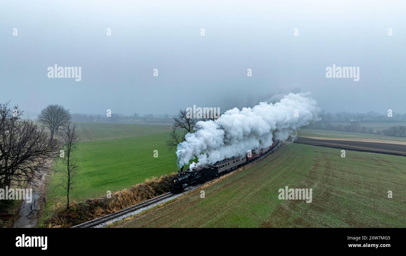 A steam train chugs through green fields, releasing clouds of smoke ...