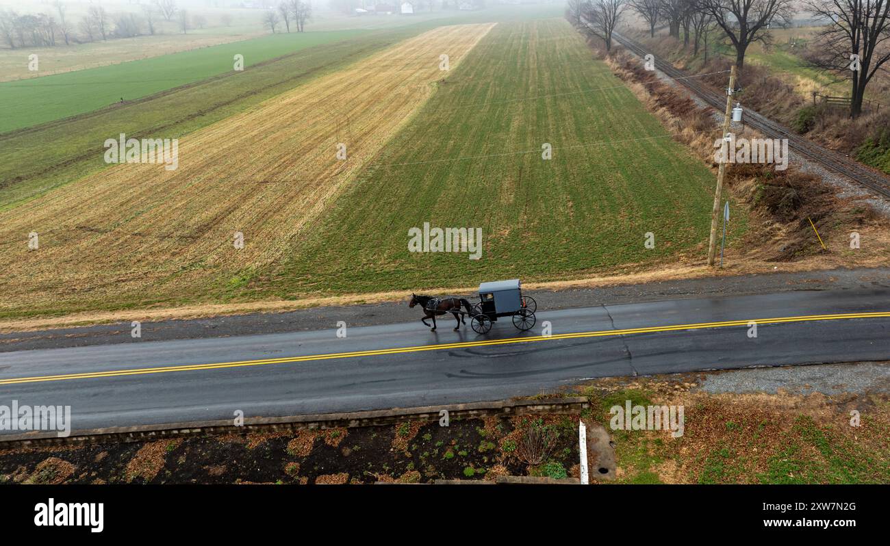 A horse-drawn Amish carriage moves steadily down a rural road ...