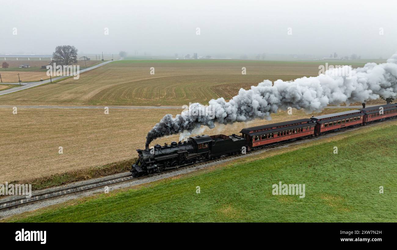 A steam locomotive chugs along railway tracks, releasing clouds of ...