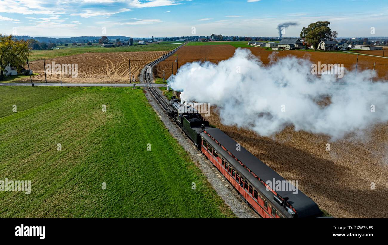 A vintage steam train puffs white smoke as it moves through green and ...