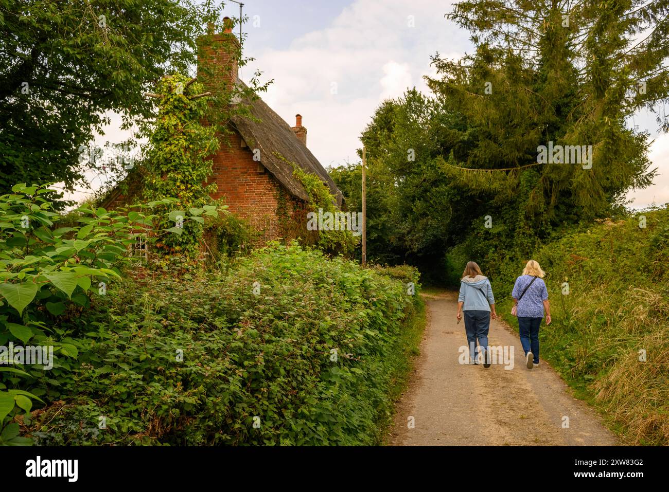 Two women friends walking past a thatched cottage in the English ...