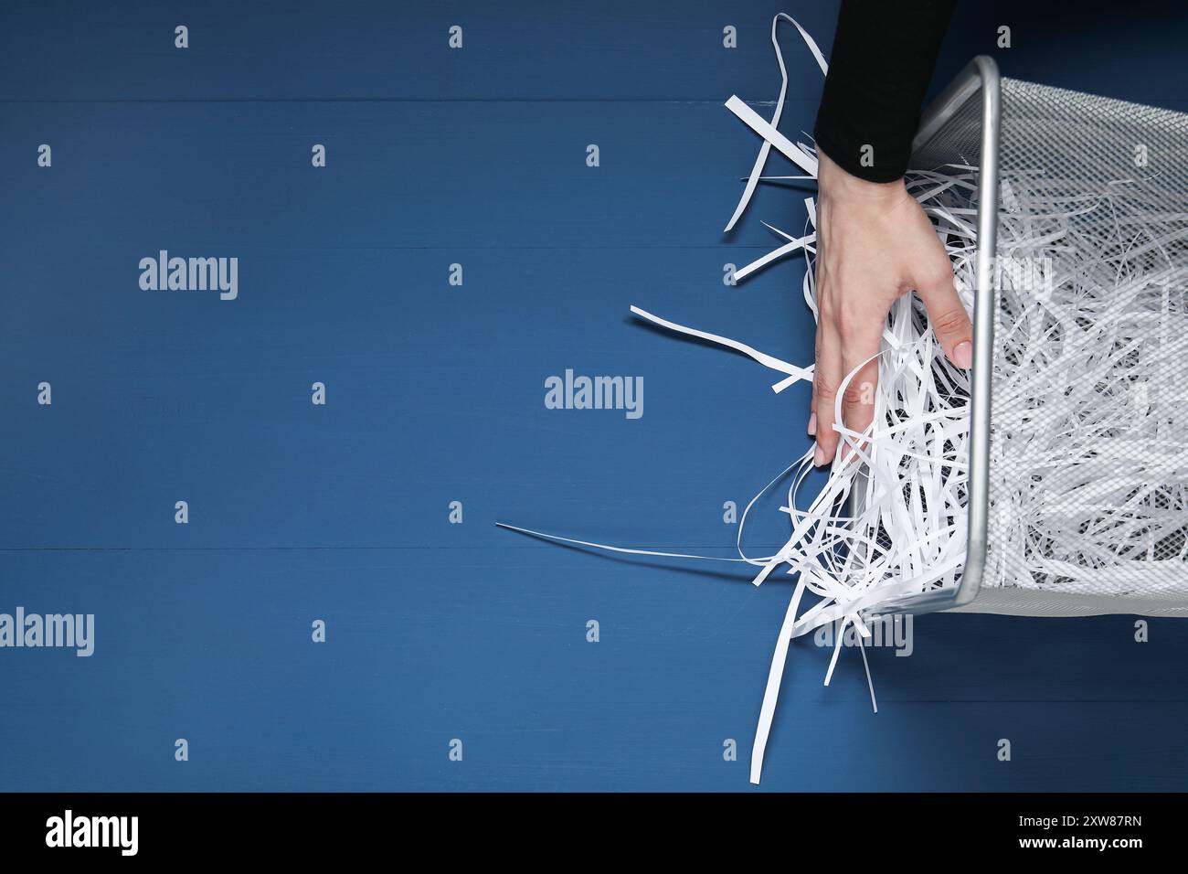Woman putting shredded paper strips into trash bin at blue wooden table ...