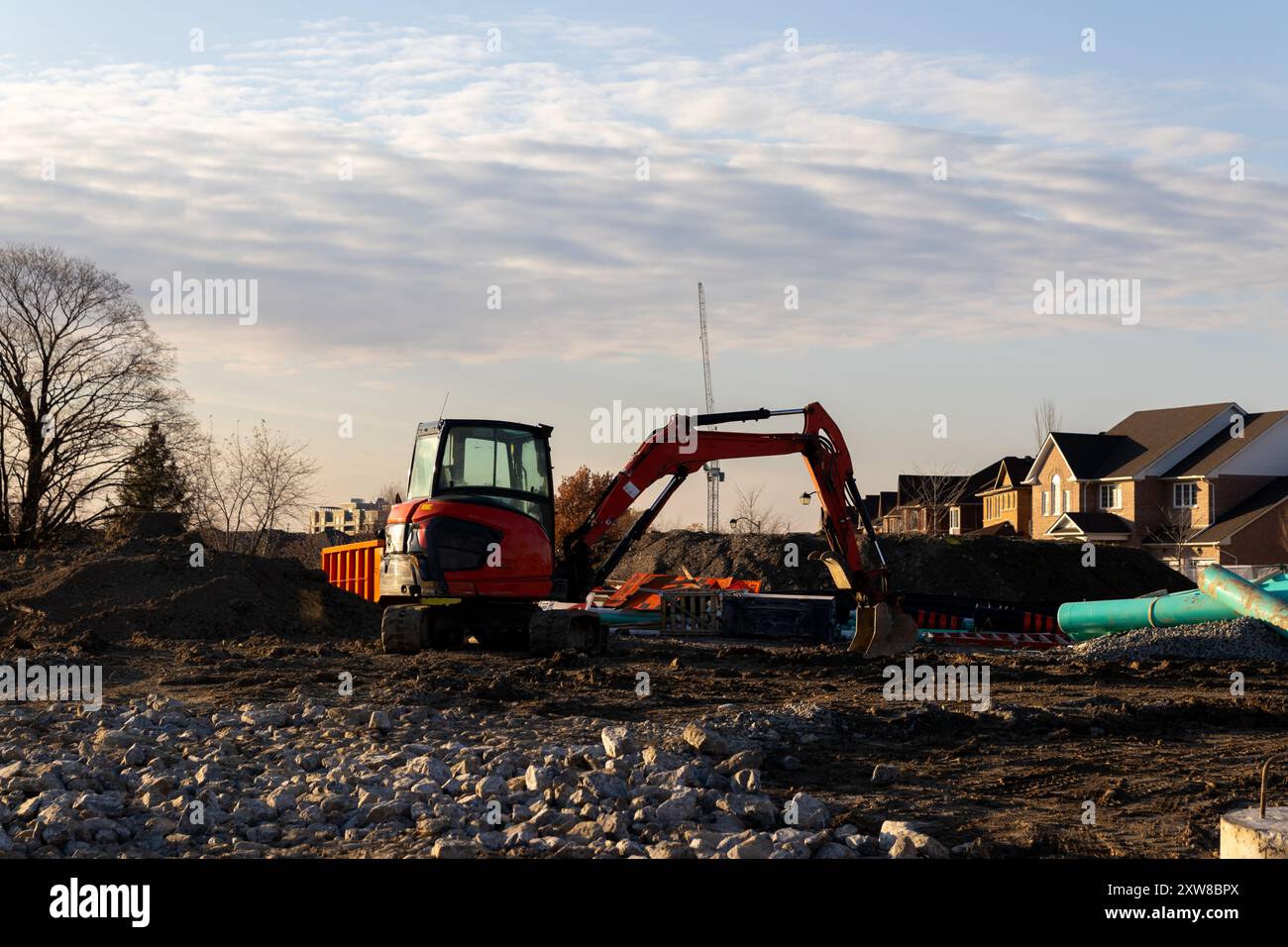 Sunset-lit construction site with red excavator amidst piles of gravel ...