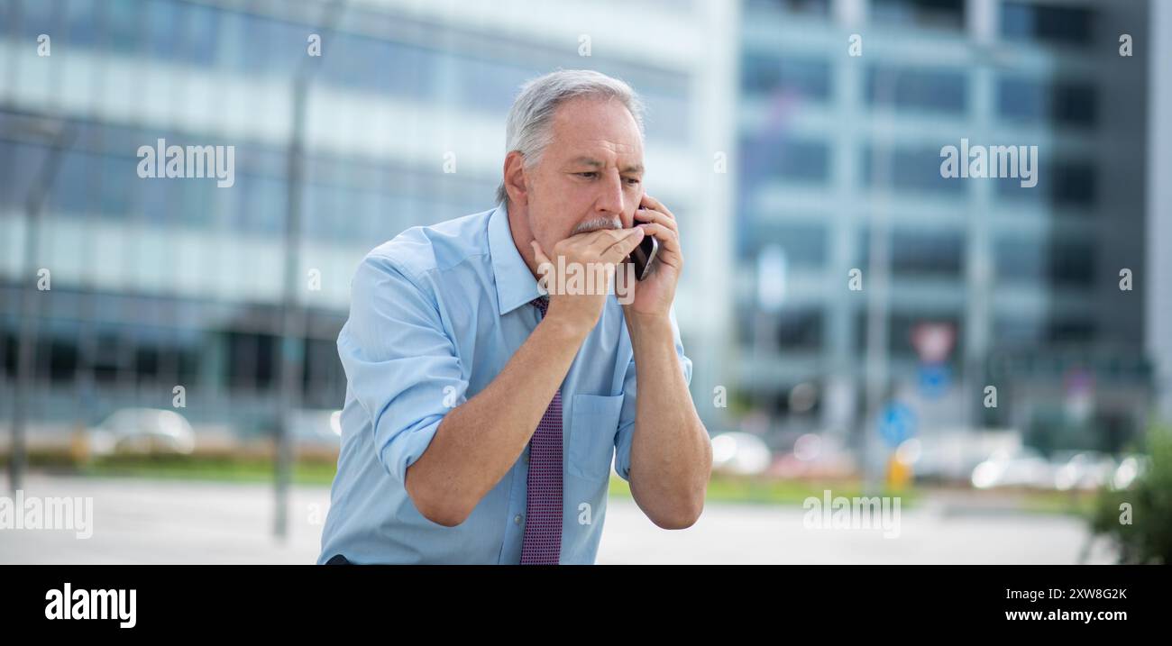 Angry senior business man yelling at the phone and biting his hand ...