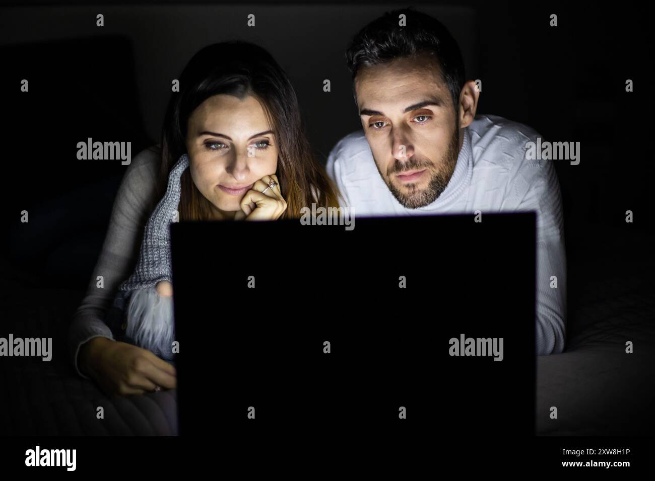 Portrait of a cheerful young couple using laptop computer while laying ...