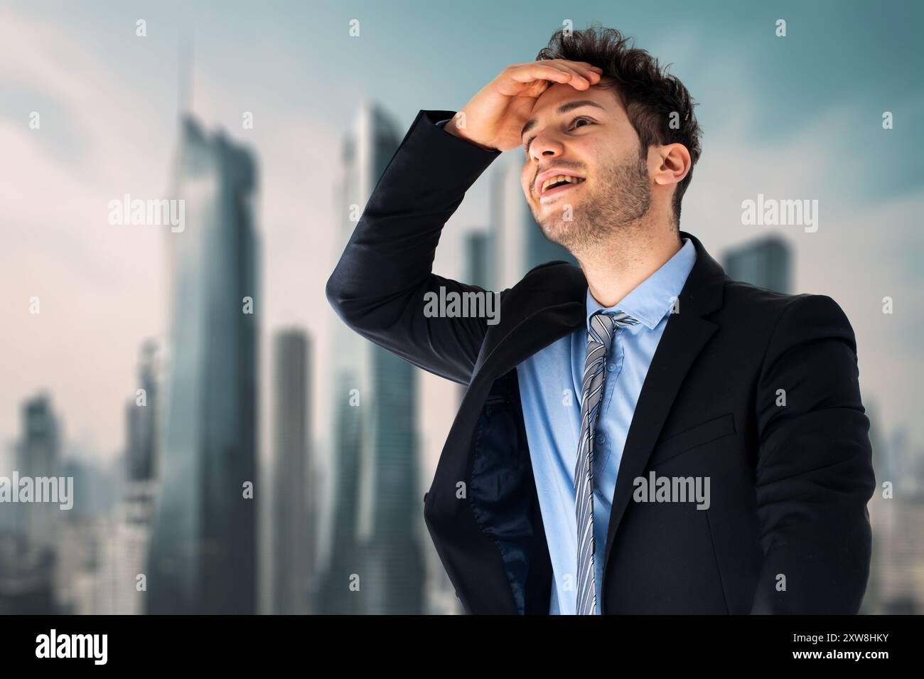 Young man in a suit looks ahead with hand shielding eyes, city skyline ...