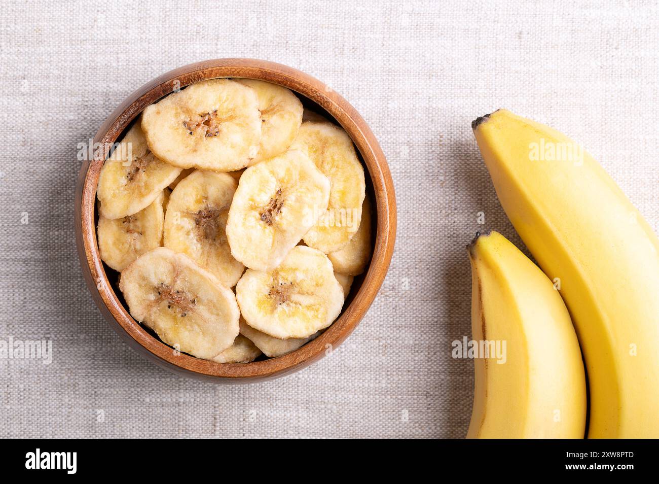 Banana chips or banana crisps in a wooden bowl on linen fabric. Yellow ...
