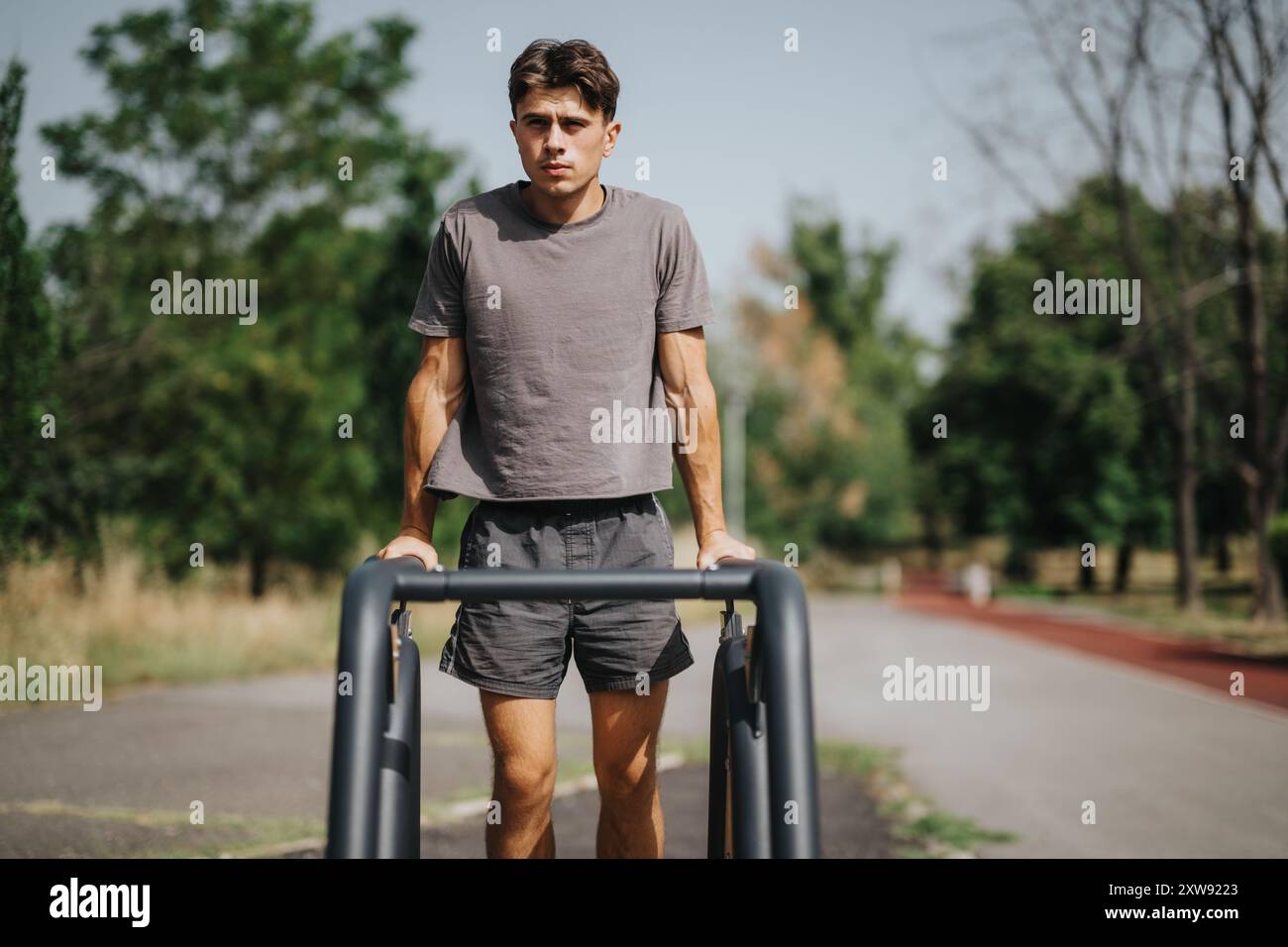 Focused young man working out on parallel bars in an outdoor park ...