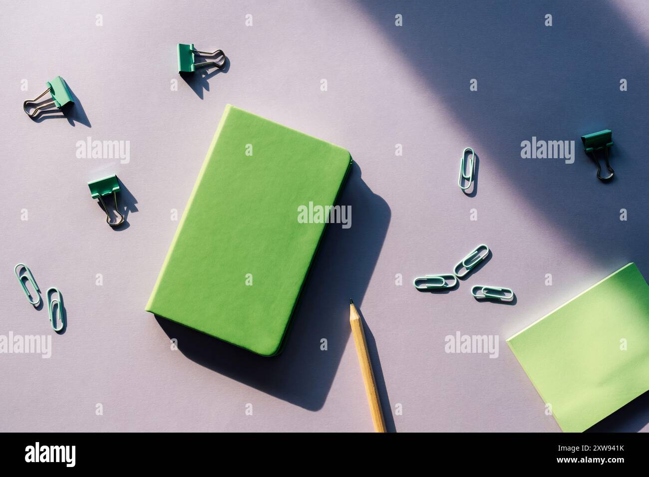 Green notepad, pencil and stationery on lilac background. Top view ...