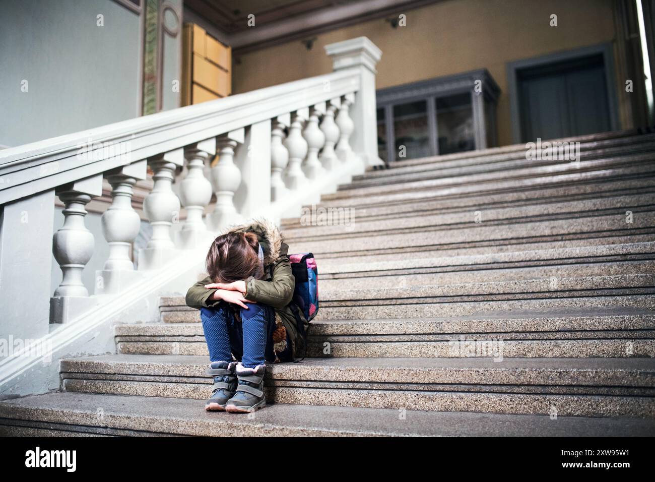 Portrait of bullied girl is crying on the steps in front of the school ...