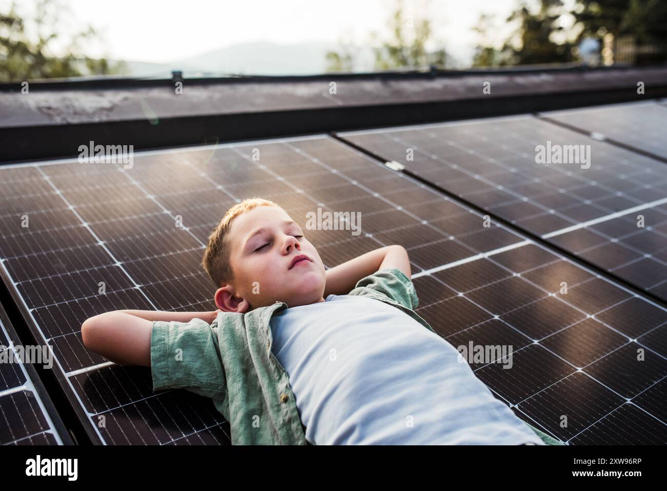 Boy lying on roof with solar panels, closed eyes. Rooftop solar or ...