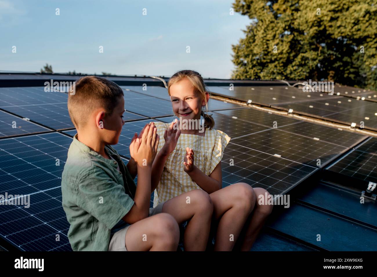 Two young siblings sitting on roof with solar panels, looking at each ...