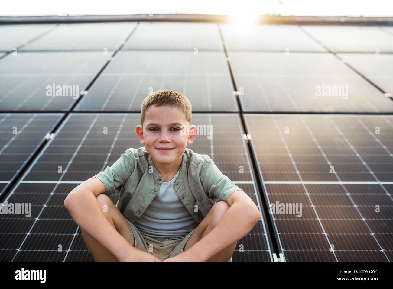 Cute boy sitting on roof with solar panels, looking at camera. Rooftop ...