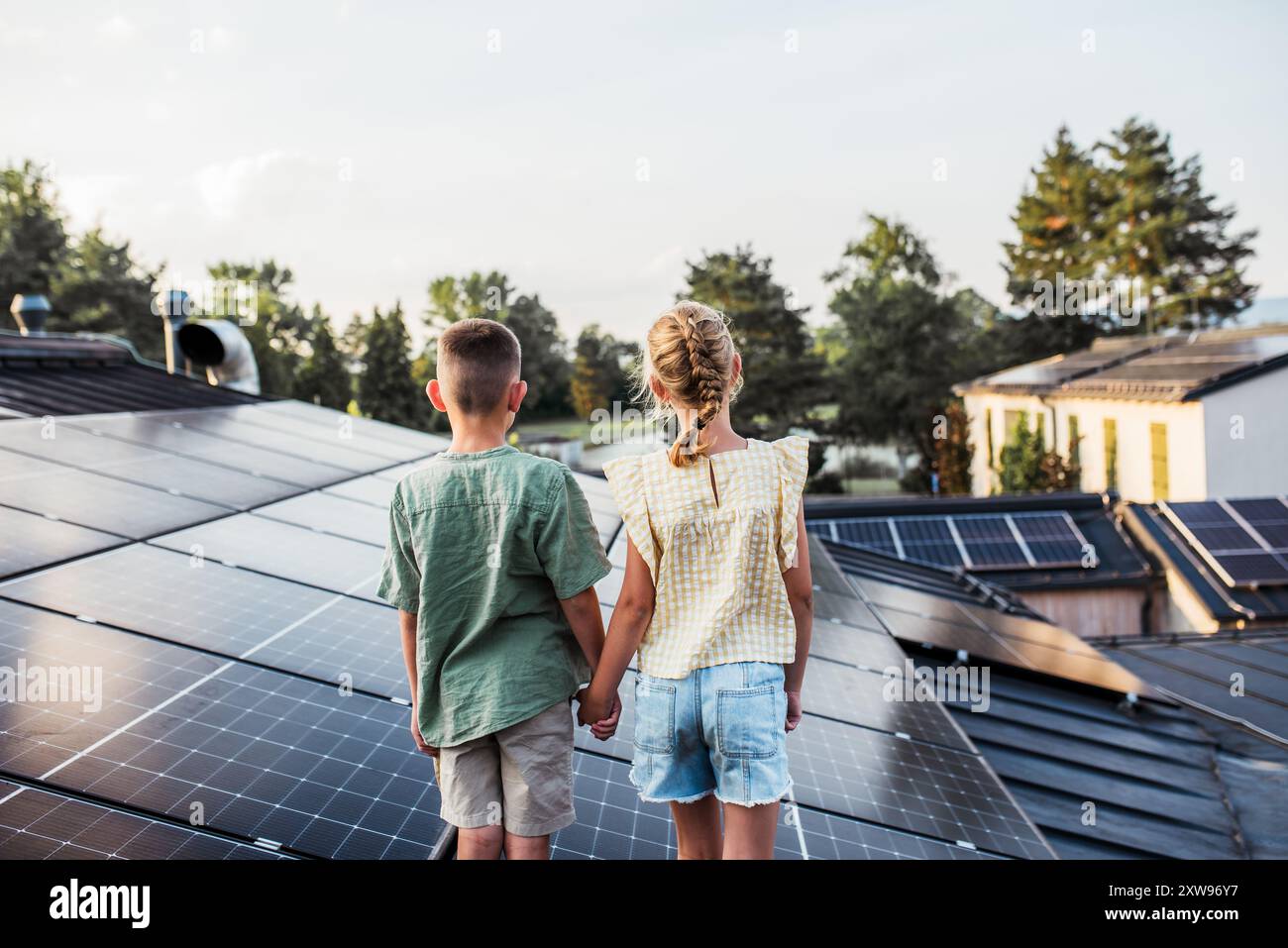 Two young siblings on roof with solar panels, holding each other ...