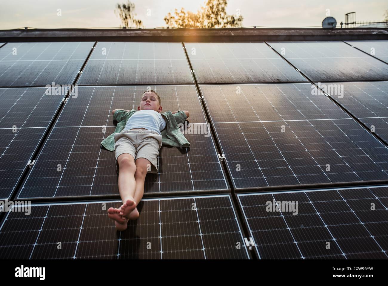 Boy lying on roof with solar panels, closed eyes. Rooftop solar or ...
