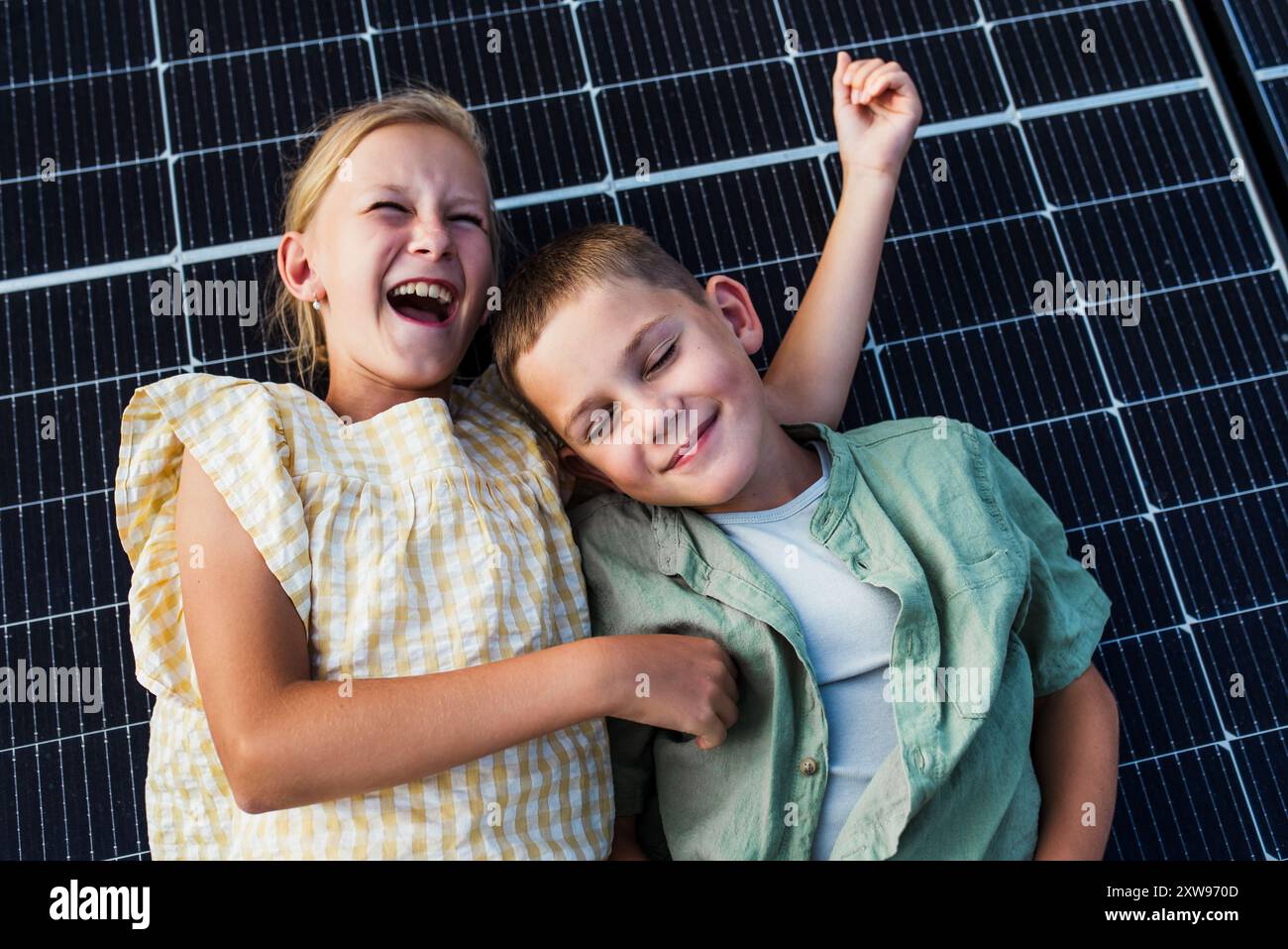 Top view of two young siblings lying on roof with solar panels. Rooftop ...