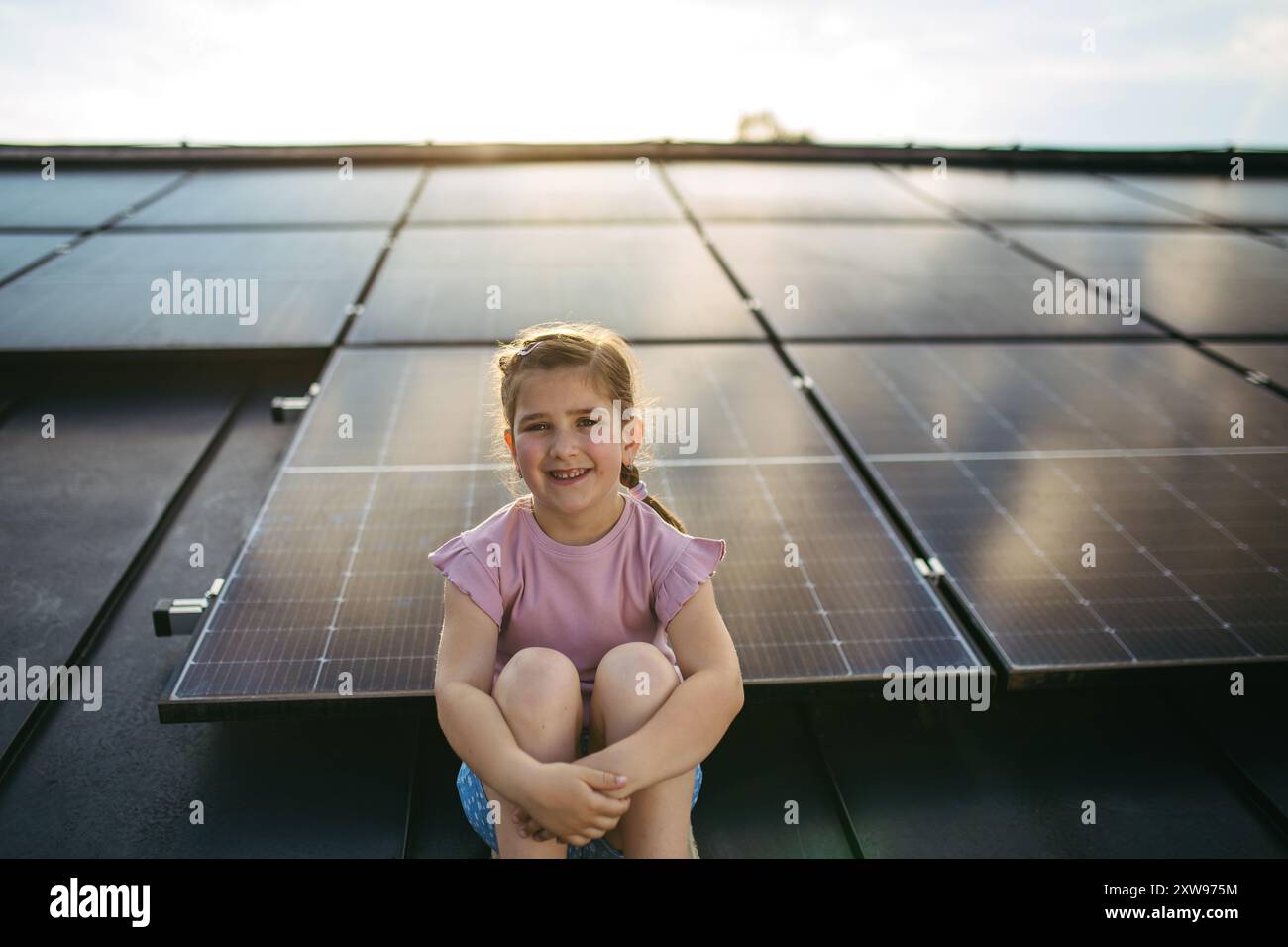 Cute girl on roof with solar panels, sitting and looking at camera ...