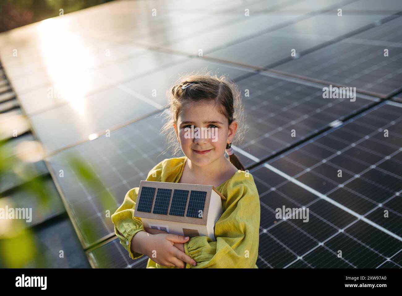 Cute girl holding model of house with solar panels, sitting on rooftop ...