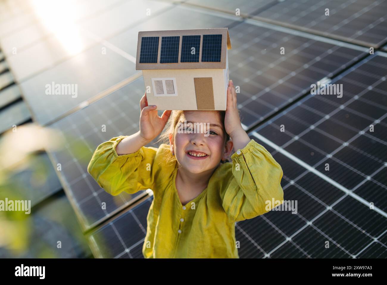 Cute girl holding model of house with solar panels, sitting on rooftop ...