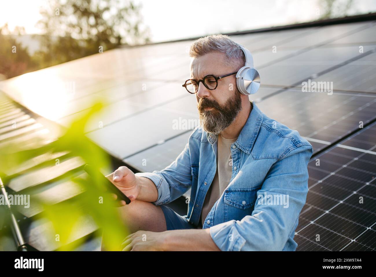 Man sitting on roof full of solar panels, headphones on head, holding ...