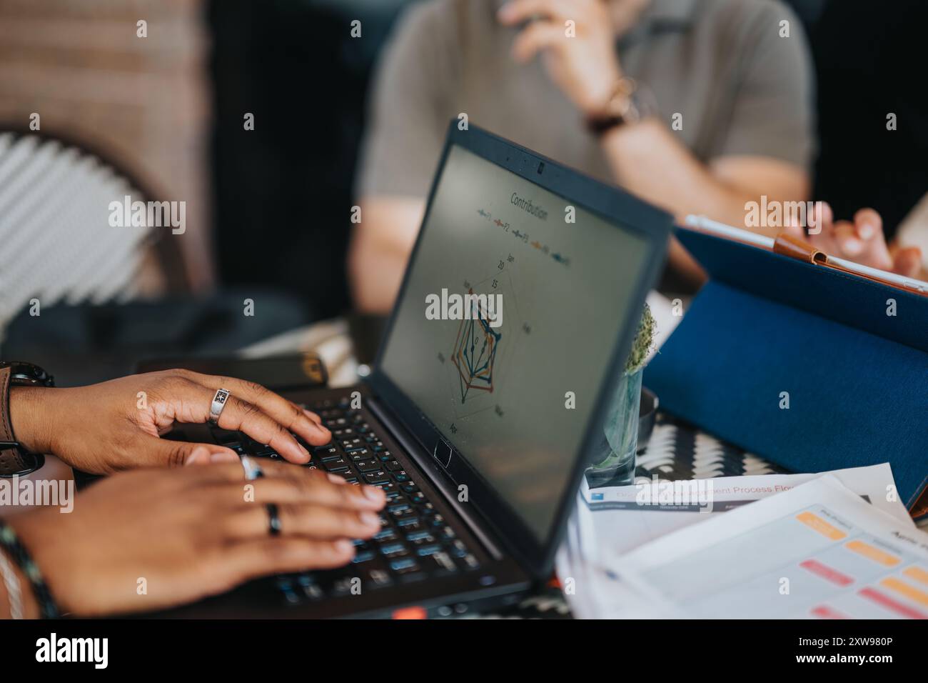 Hands typing on laptop in a business meeting with charts and documents ...