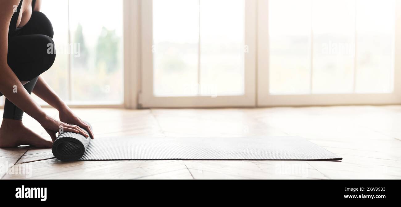 Side view of woman rolling her yoga mat before training Stock Photo - Alamy