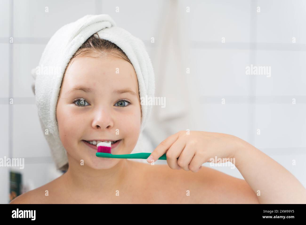 Morning routines: Little teenage girl brushing her teeth with a green toothbrush in a white ...