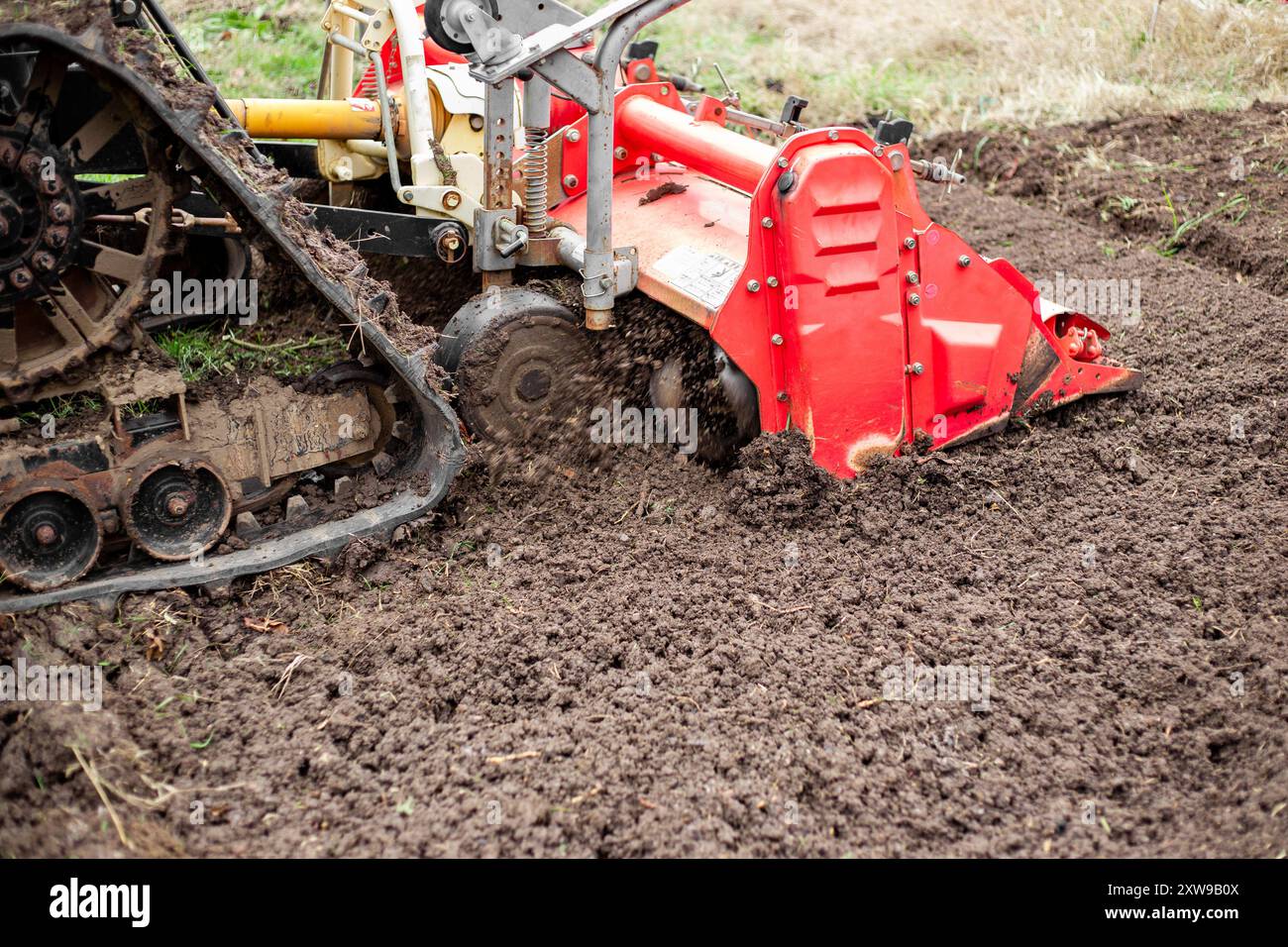 A mini tractor with a milling machine plows the ground on an ...