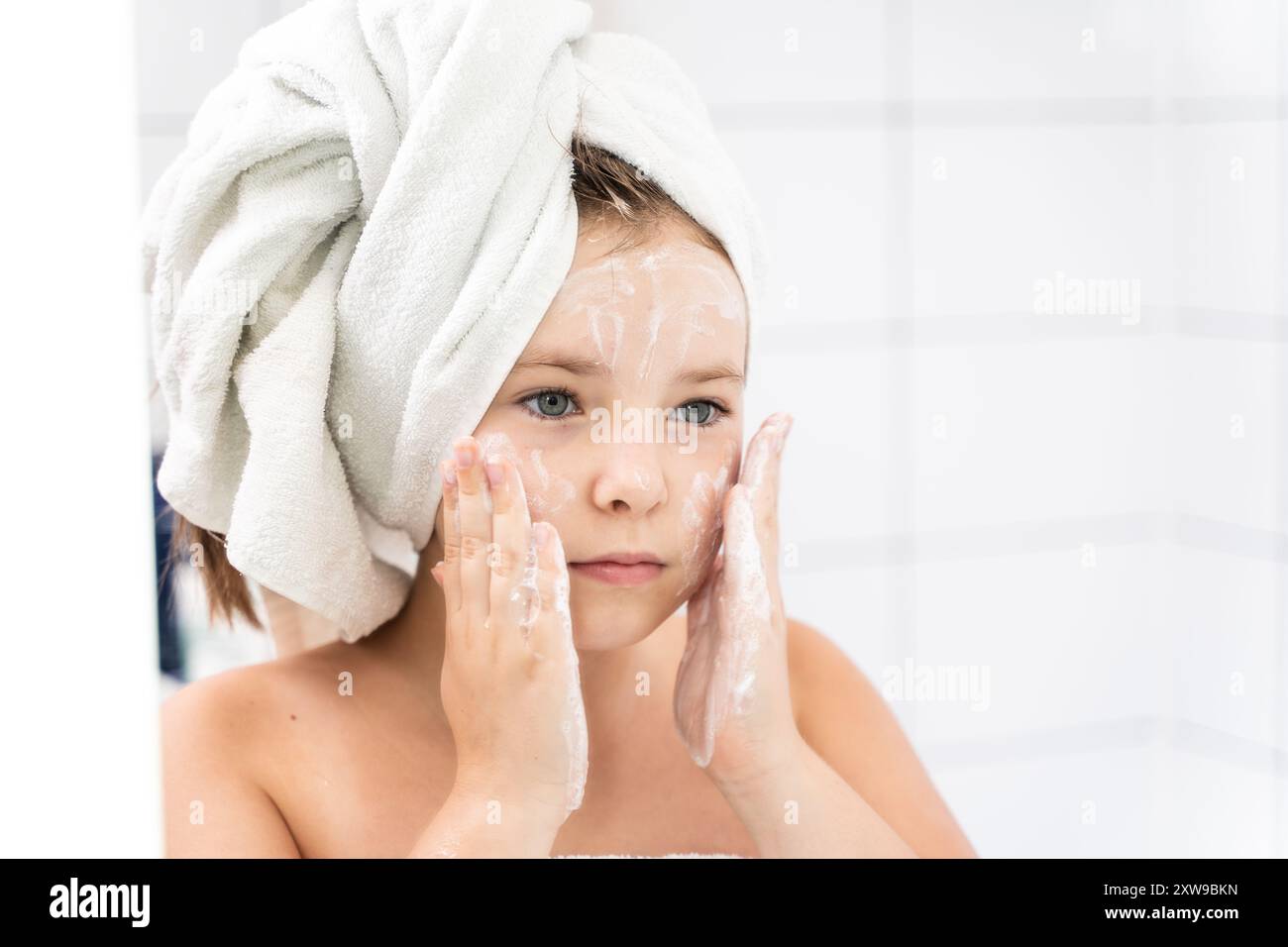Little teen girl washing her face with acne foam in white bathroom ...