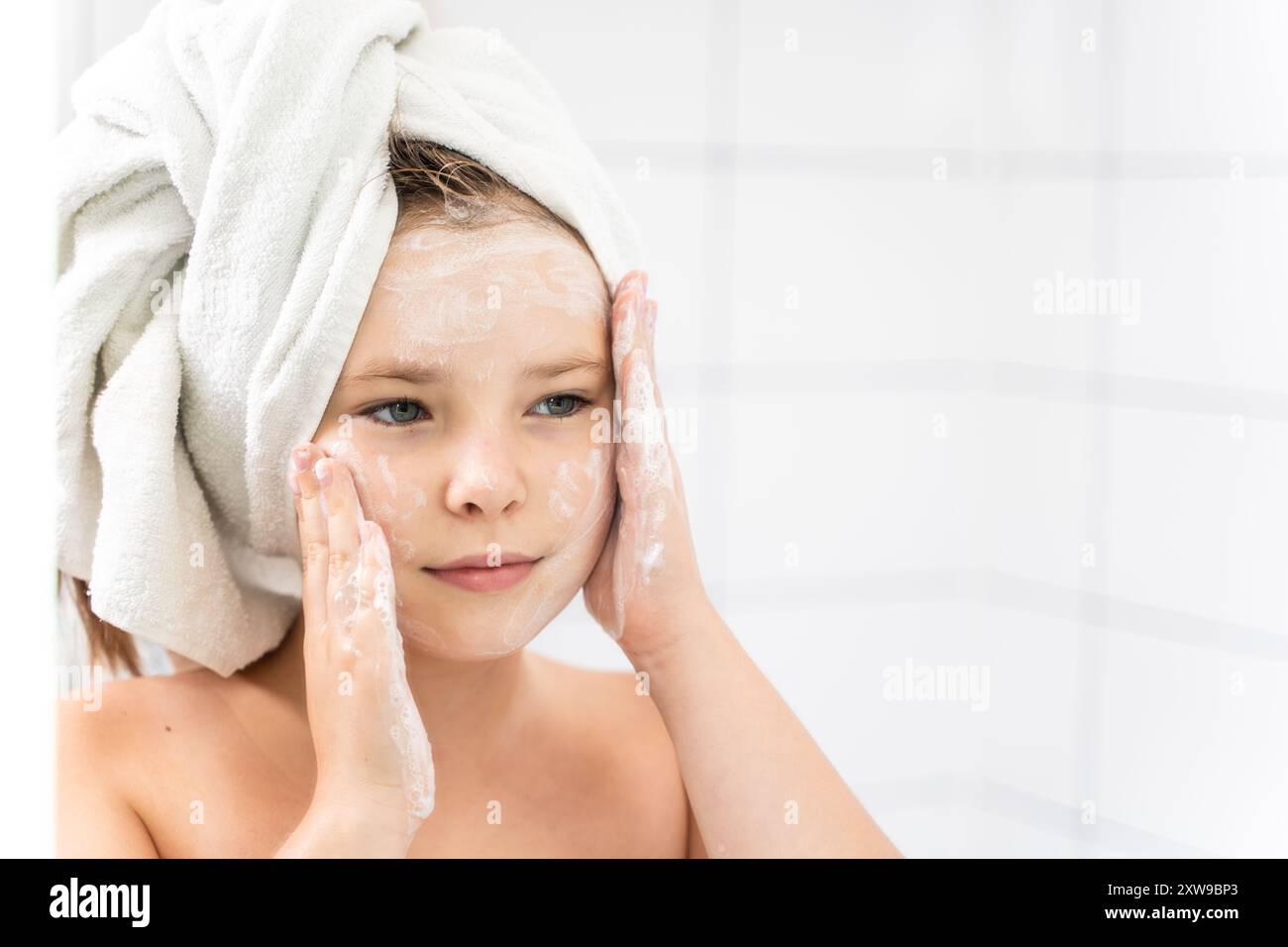 Little teen girl washing her face with acne foam in white bathroom ...