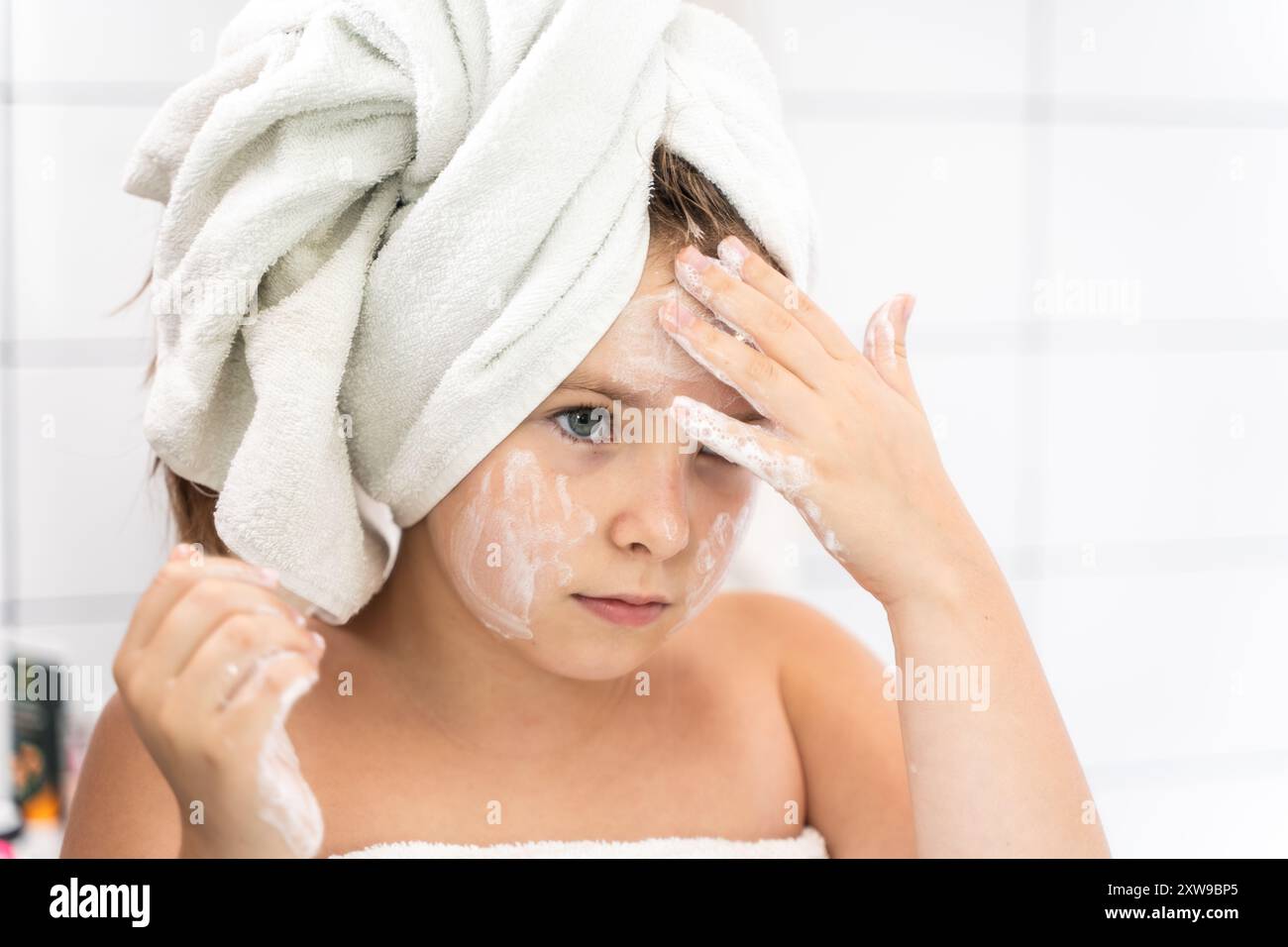 Little teen girl washing her face with acne foam in white bathroom ...